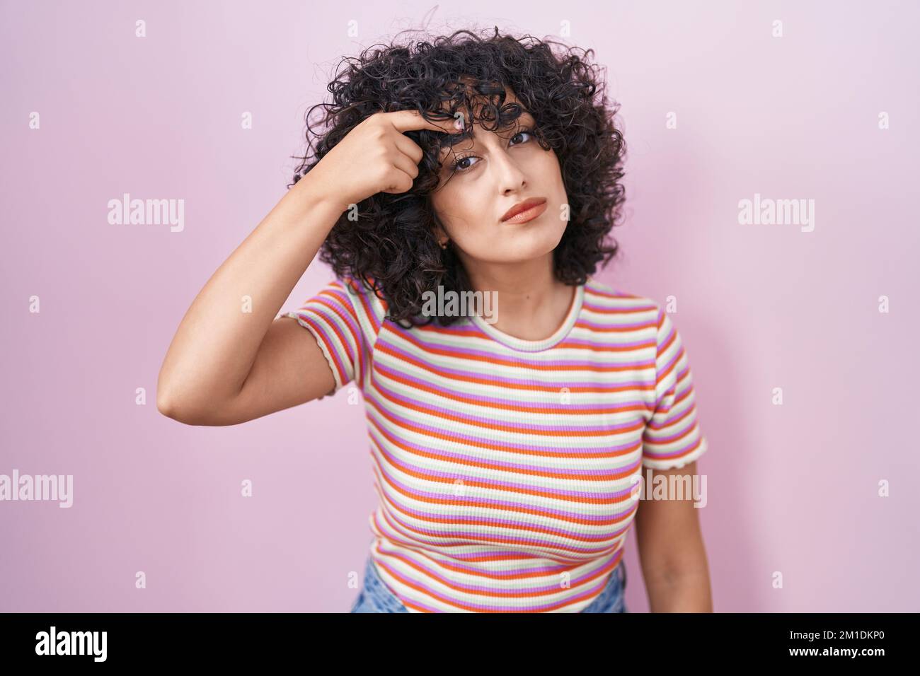 Young middle east woman standing over pink background pointing unhappy ...