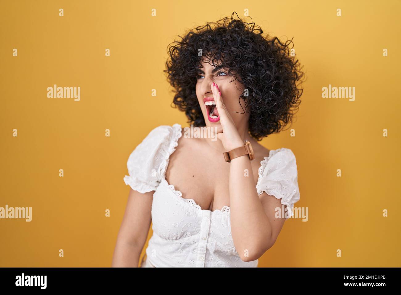 Young brunette woman with curly hair standing over yellow background ...