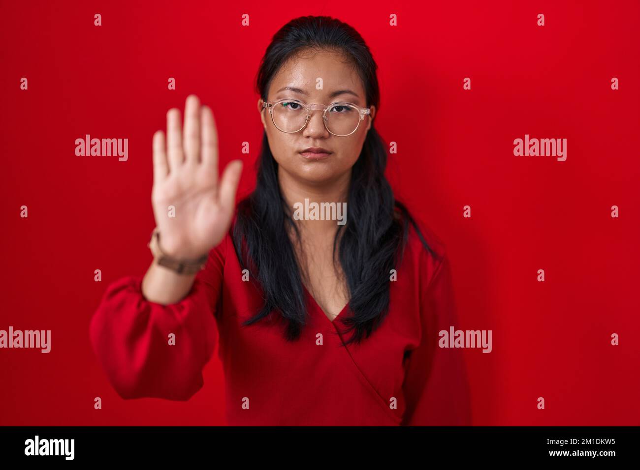 Asian young woman standing over red background doing stop sing with ...
