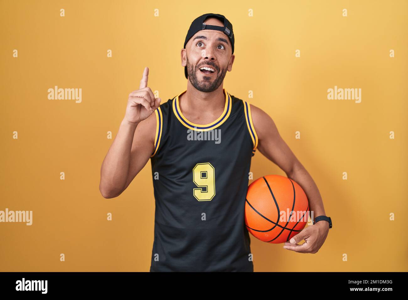 Middle age bald man holding basketball ball over yellow background ...