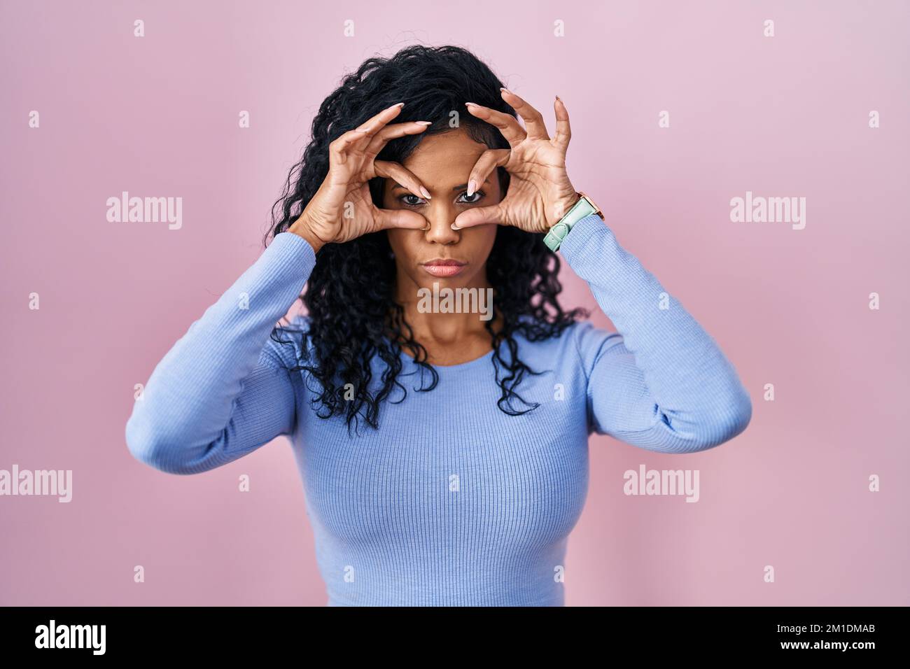 Middle age hispanic woman standing over pink background trying to open ...