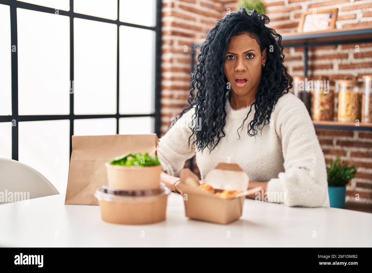 Middle age hispanic woman eating take away food scared and amazed with ...