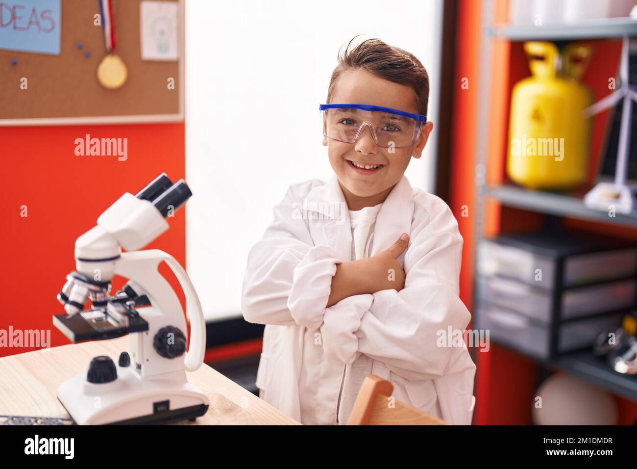 Adorable hispanic toddler student using microscope standing with arms ...