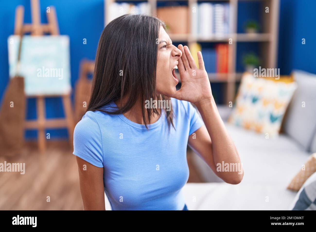 Brunette young woman sitting on the sofa at home shouting and screaming ...