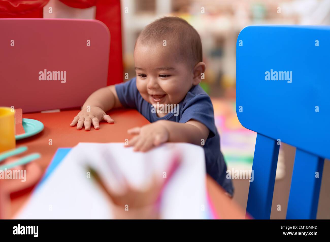 Adorable chinese toddler leaning on table standing at kindergarten ...