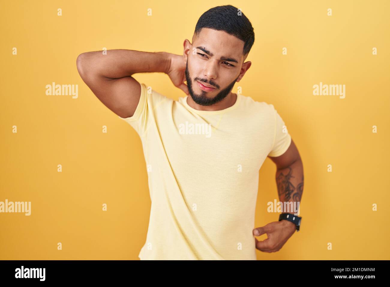 Young hispanic man standing over yellow background suffering of neck ...