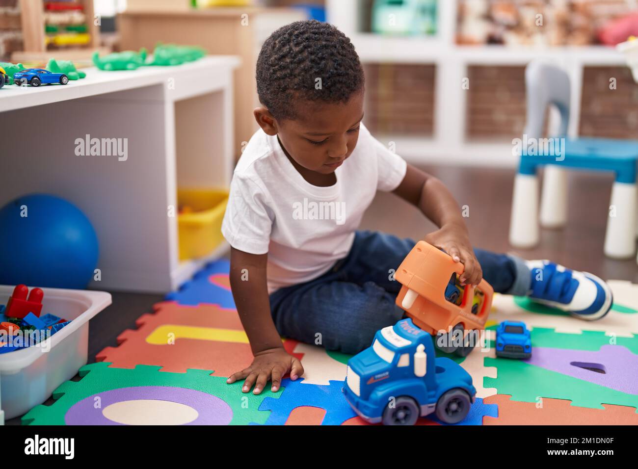 African american boy playing with cars and truck toy sitting on floor ...