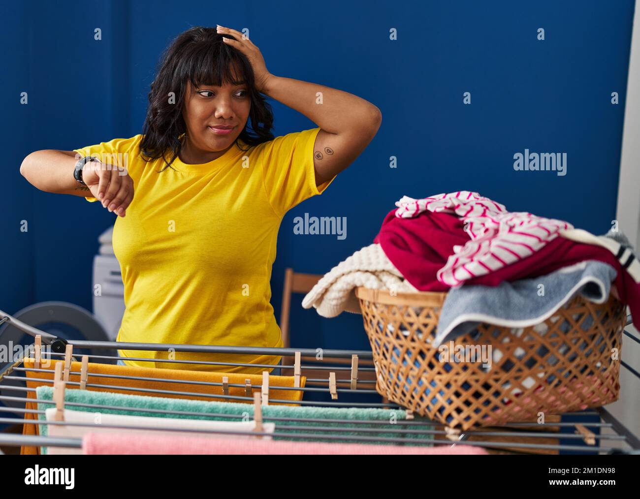 Young beautiful latin woman looking clock hanging clothes on ...