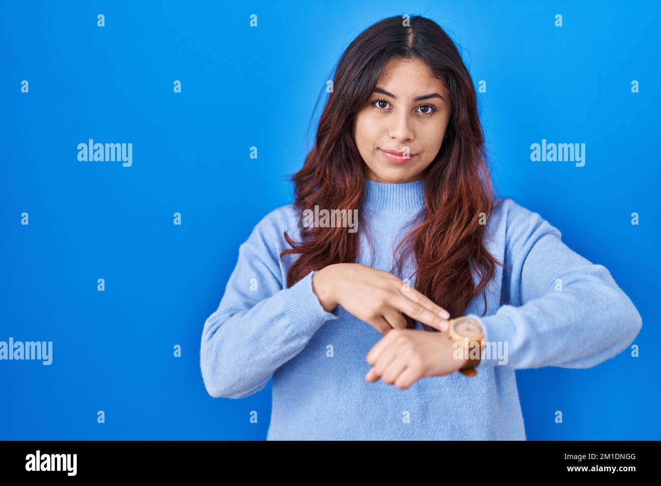 Hispanic young woman standing over blue background in hurry pointing to ...