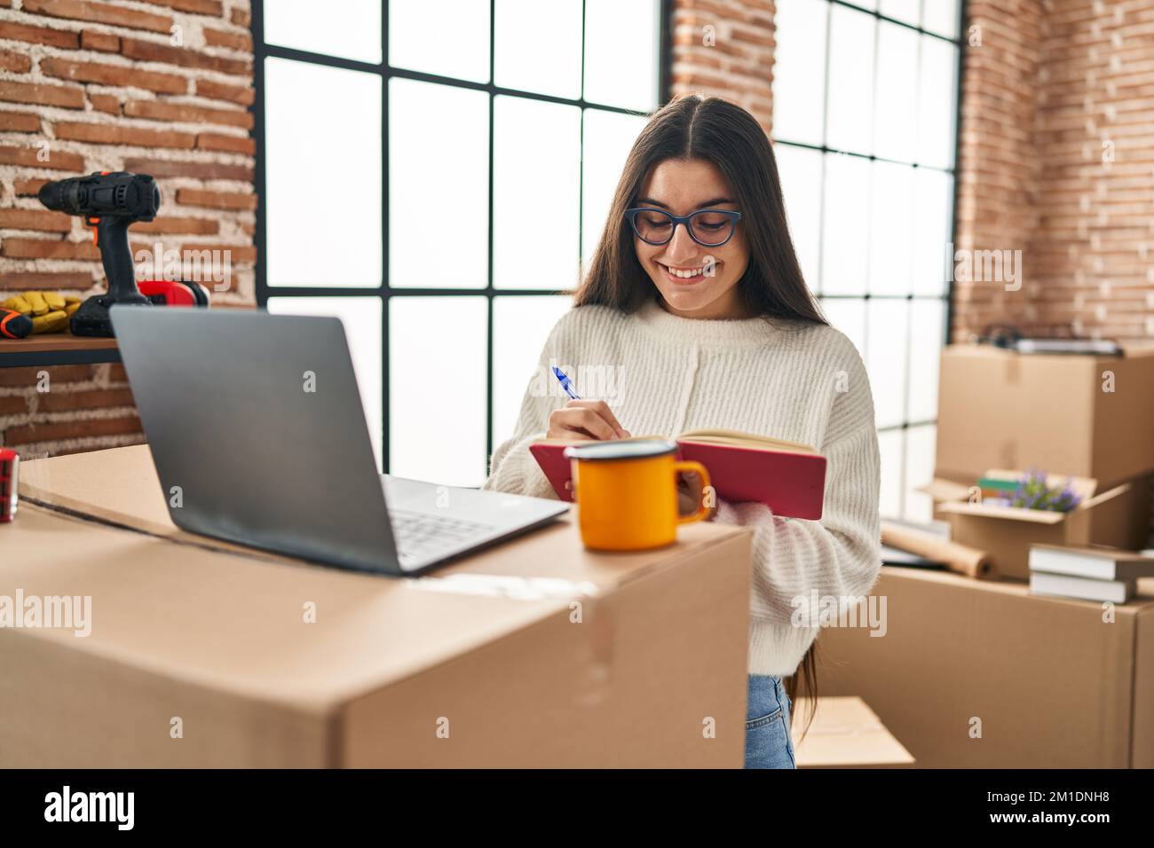 Young hispanic woman smiling confident using laptop and write on book ...