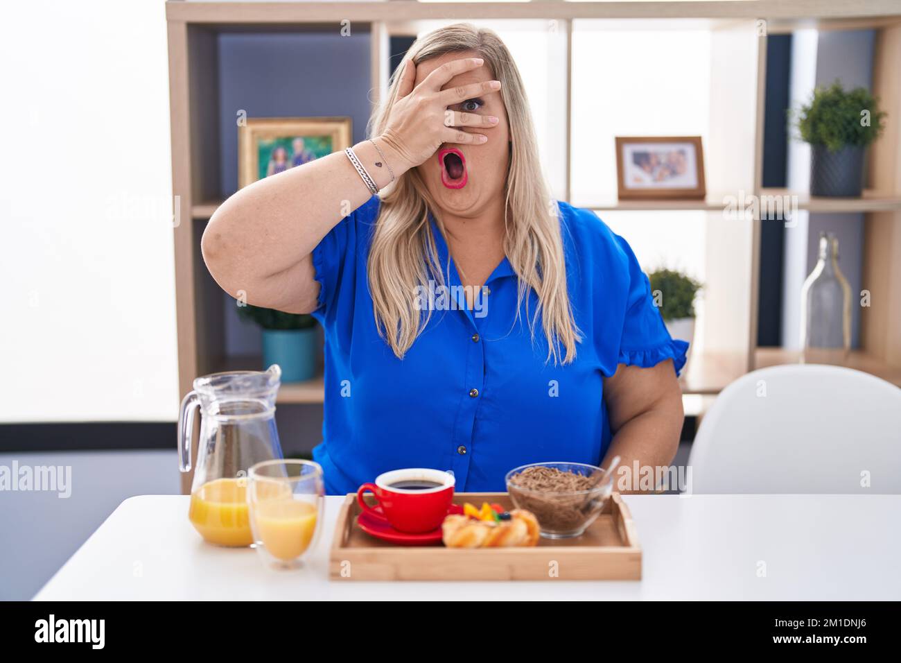 Caucasian plus size woman eating breakfast at home peeking in shock ...