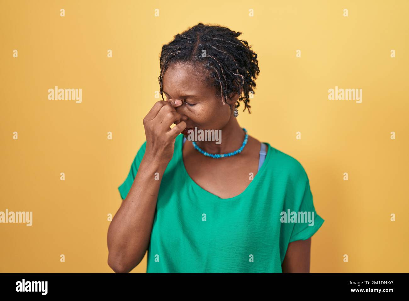African woman with dreadlocks standing over yellow background tired ...