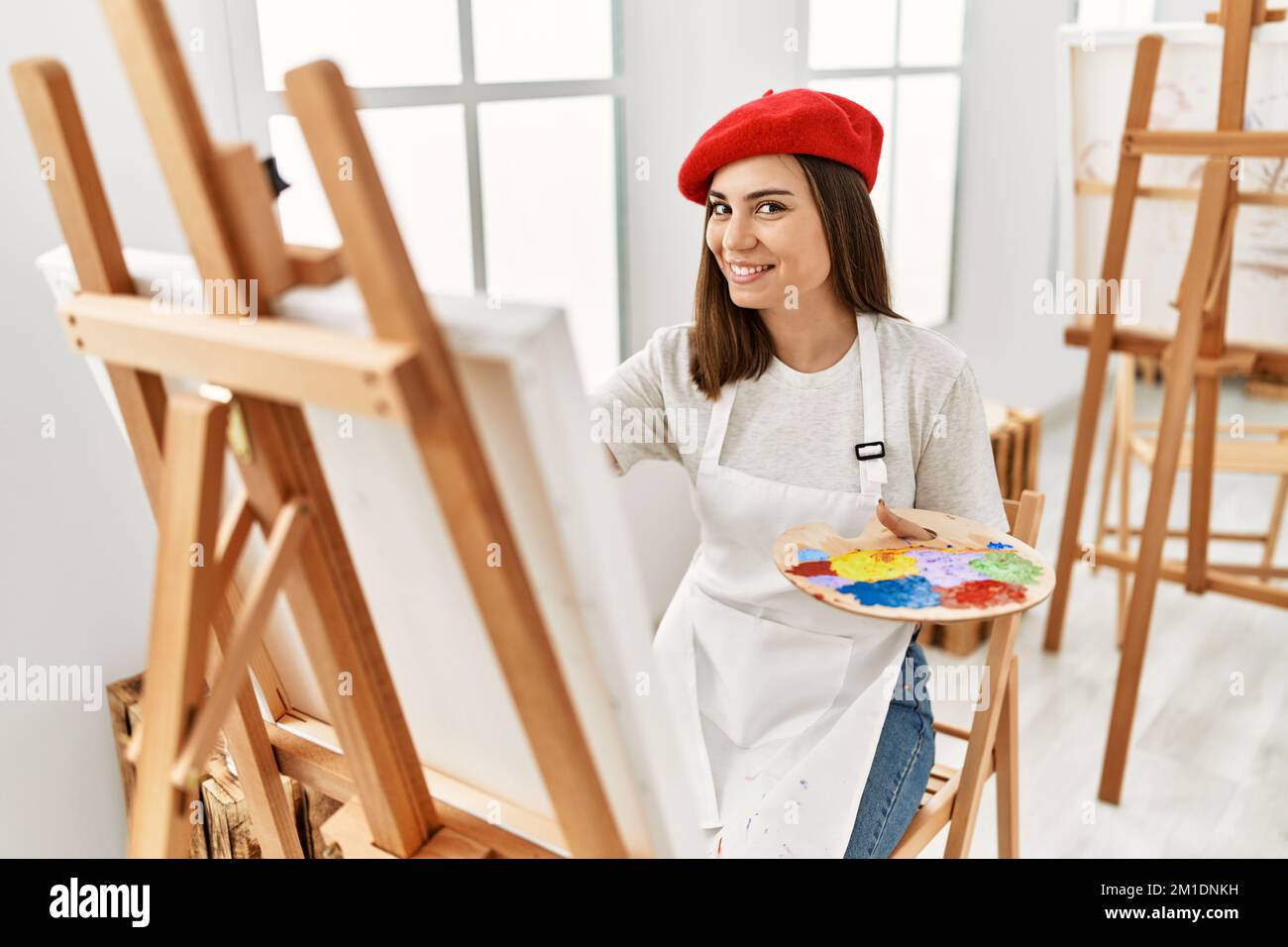 Young hispanic artist woman wearing french beret drawing at art studio ...