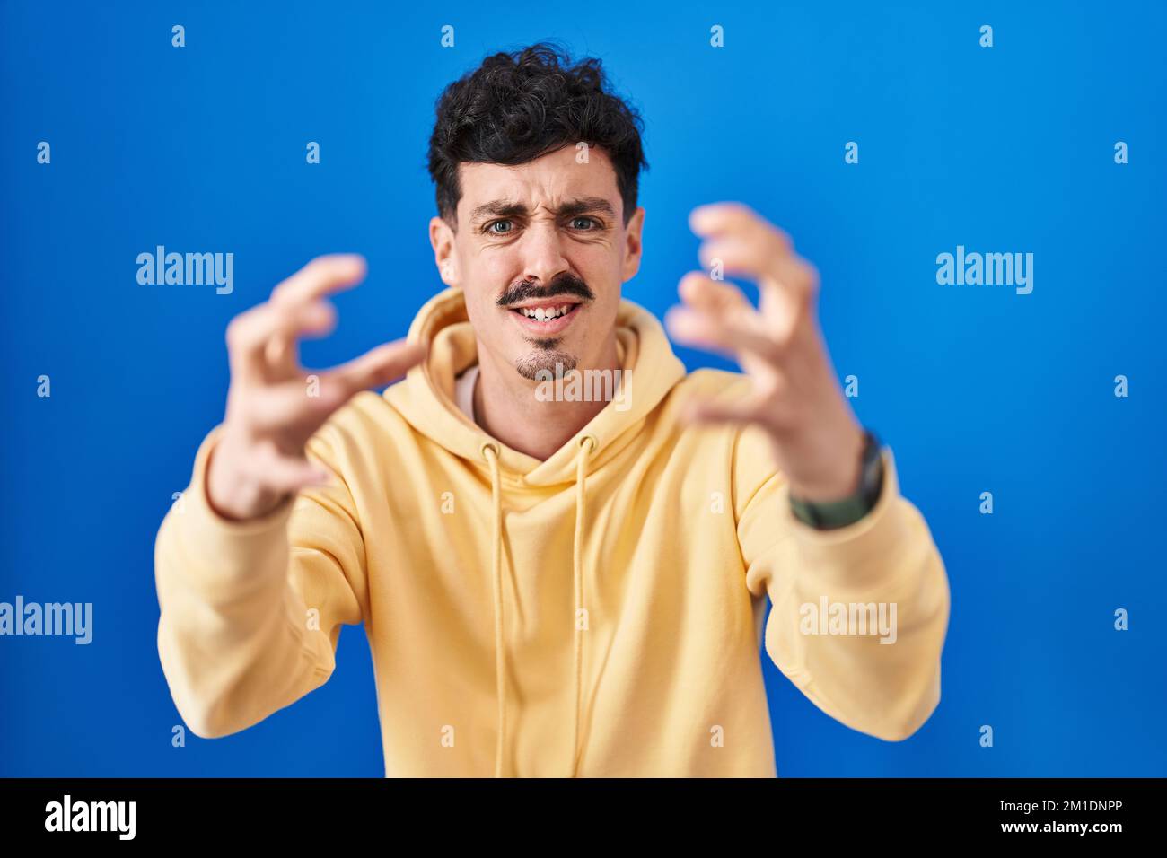 Hispanic man standing over blue background shouting frustrated with ...
