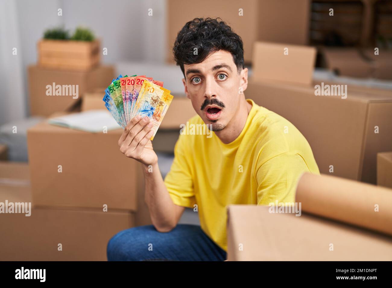 Hispanic man at new new home holding swiss francs banknotes scared and ...