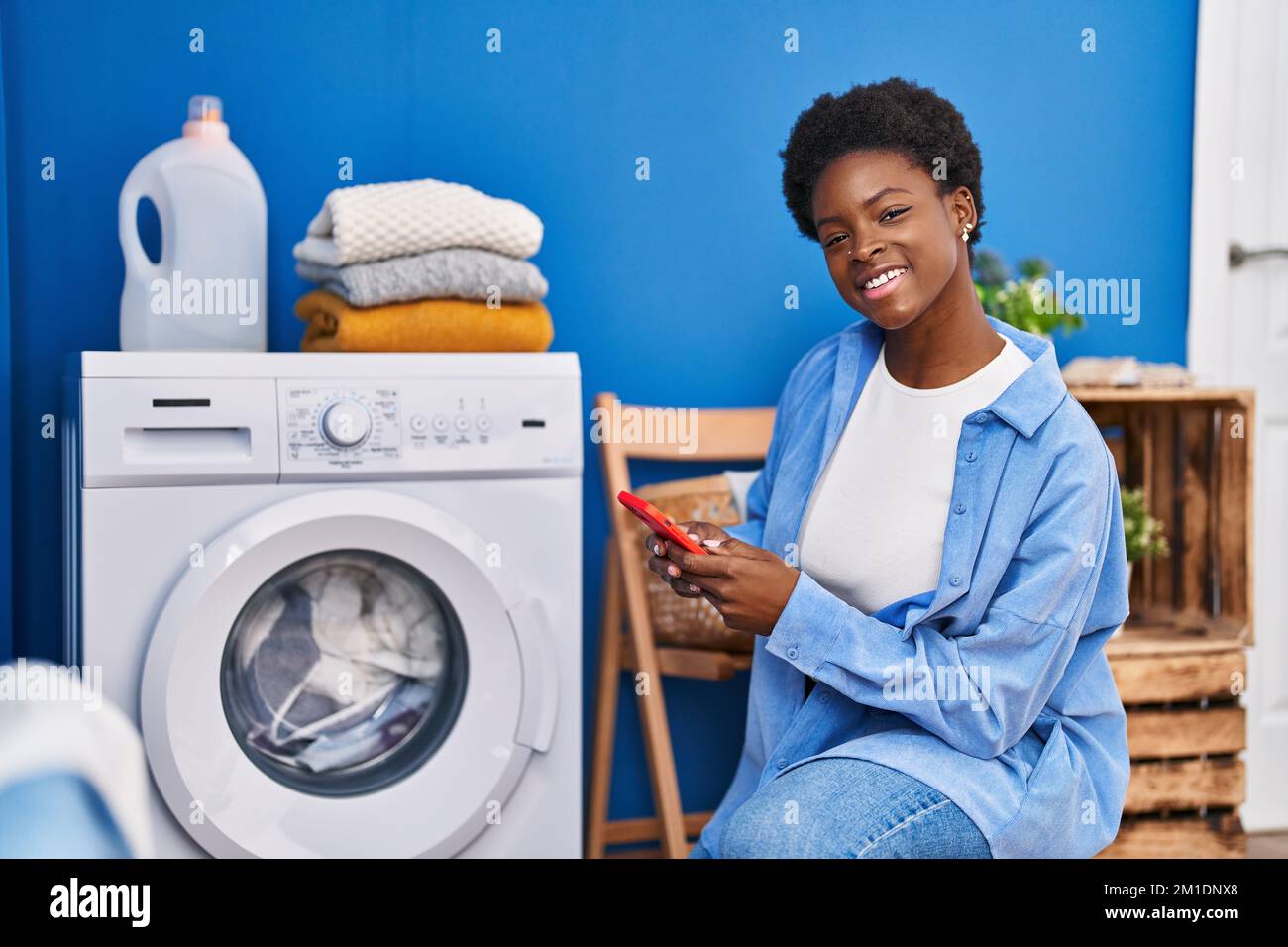 African american woman using smartphone waiting for washing machine at ...