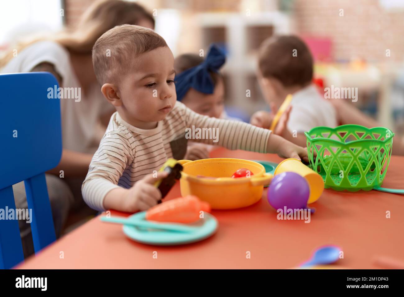 Group of toddlers learning to eat sitting on table at kindergarten ...