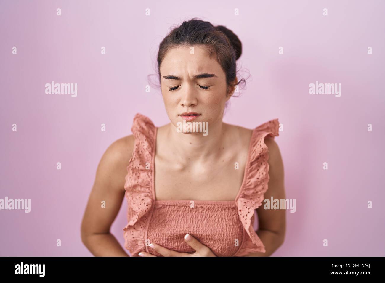 Young teenager girl standing over pink background with hand on stomach ...