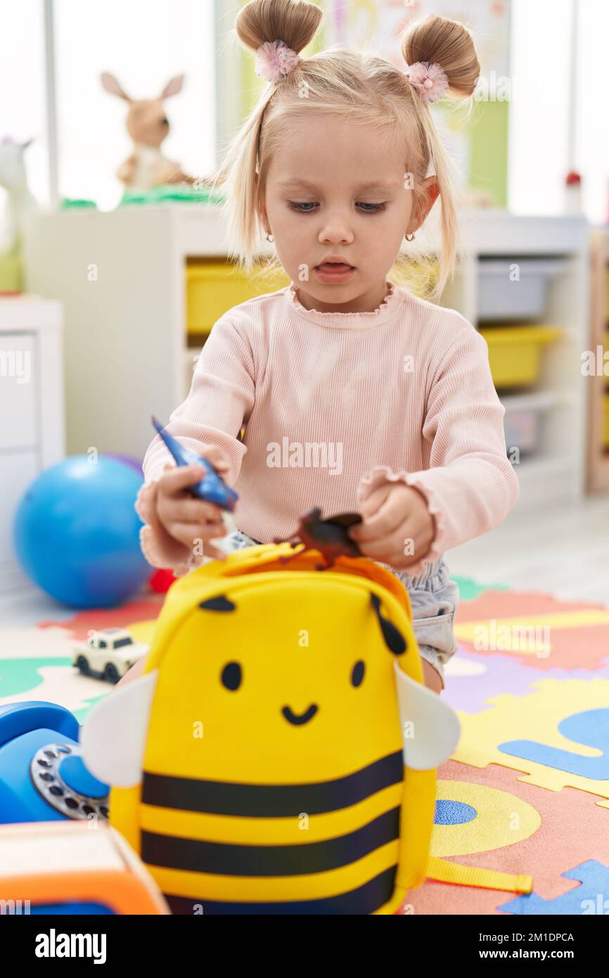 Adorable caucasian girl sitting on floor opening backpack at ...