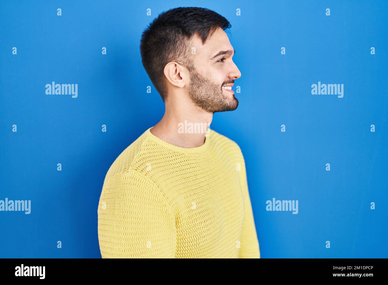 Hispanic man standing over blue background looking to side, relax ...