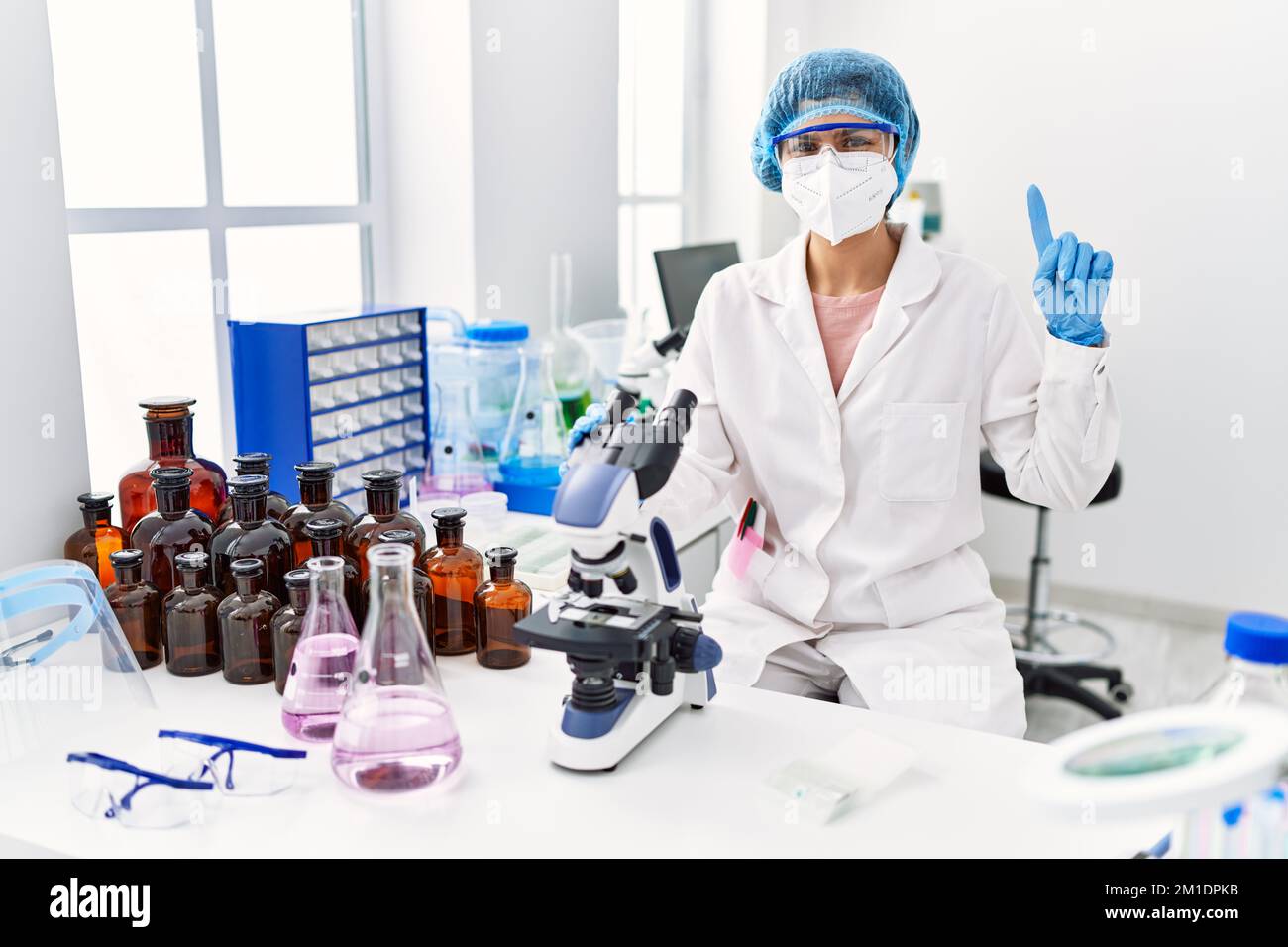 Young brunette woman working at scientist laboratory smiling with an idea or question pointing ...