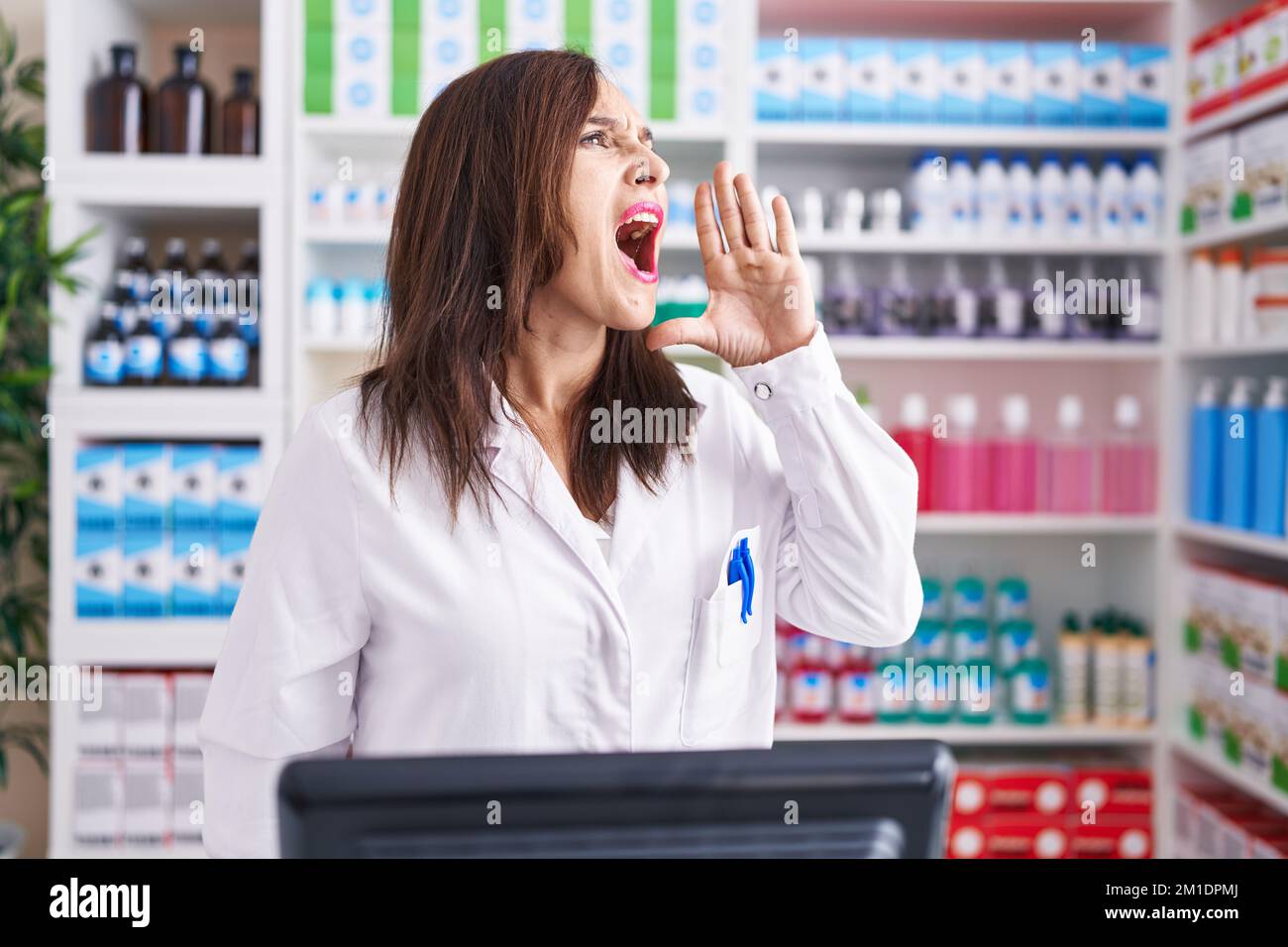 Middle age brunette woman working at pharmacy drugstore shouting and ...