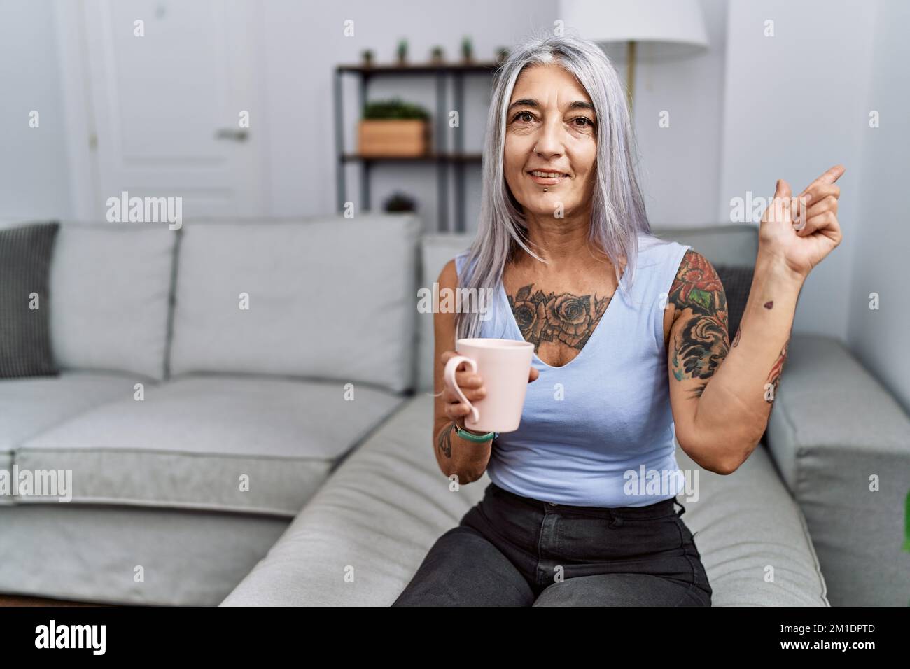 Middle age grey-haired woman drinking coffee sitting on the sofa at ...