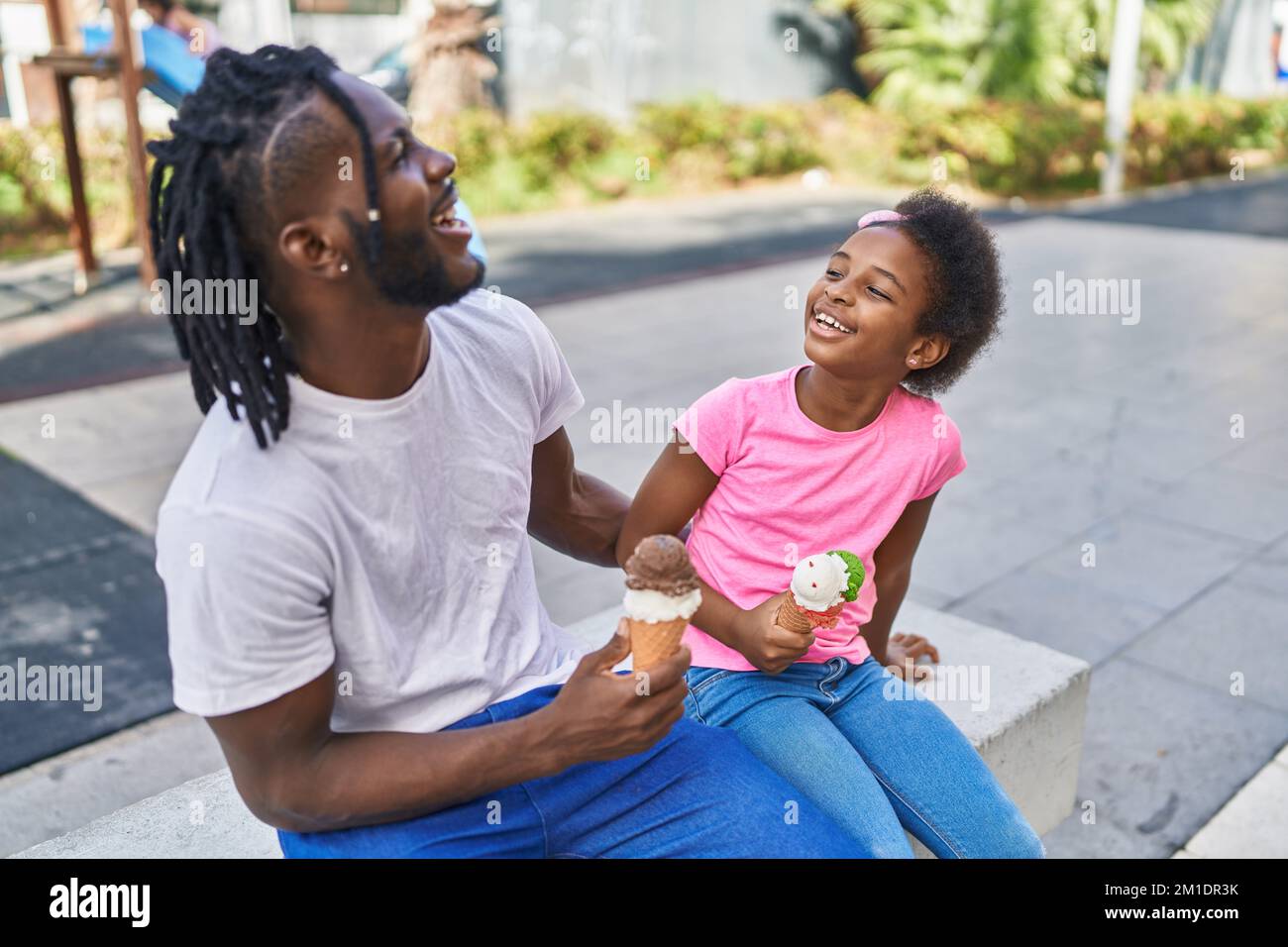 Father and daughter eating ice cream sitting together on bench at park ...