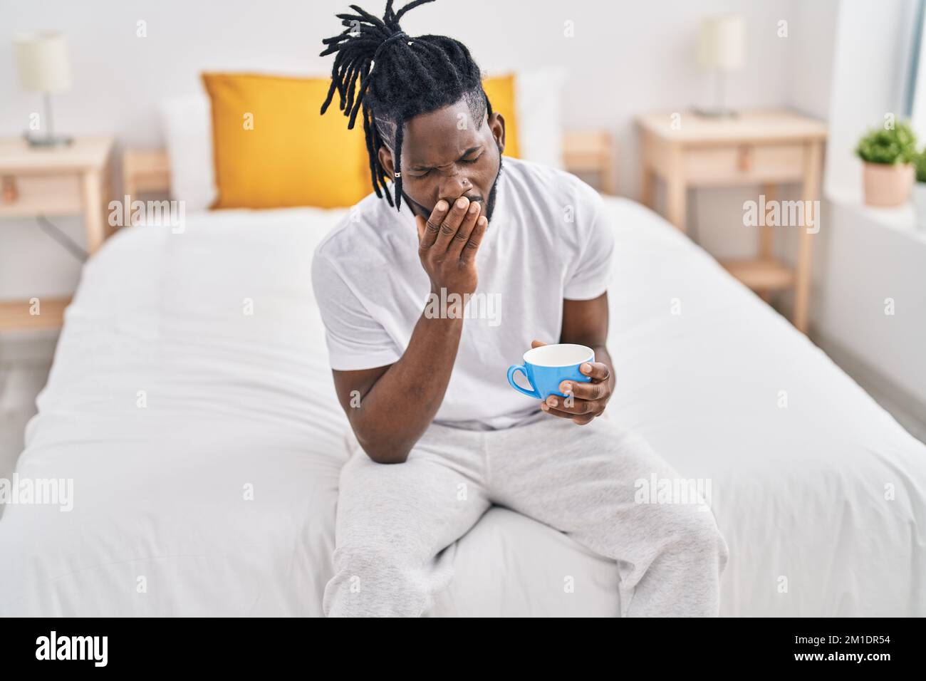 African american woman tired drinking coffee sitting on bed at bedroom ...