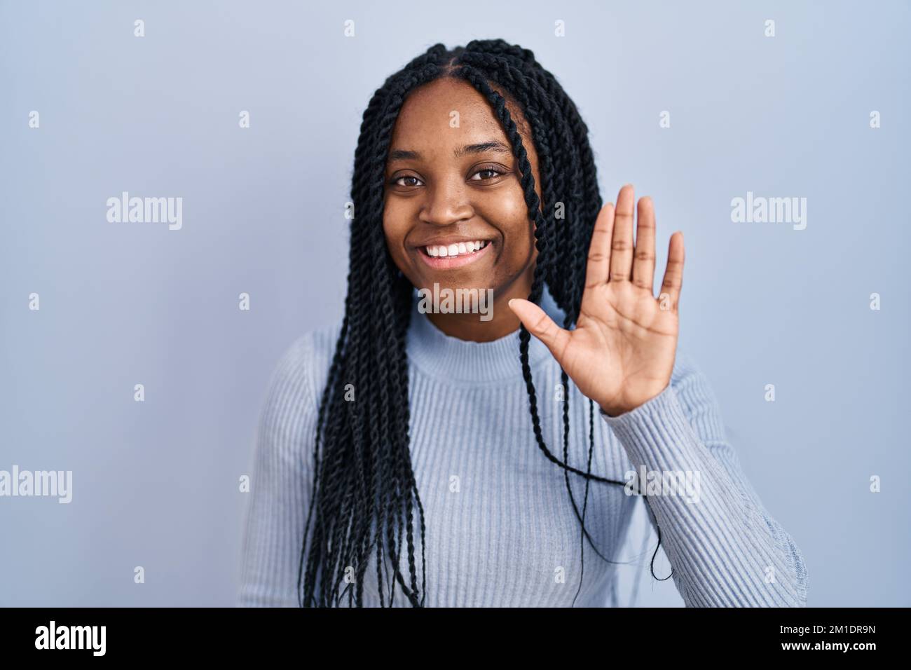 African american woman standing over blue background waiving saying ...