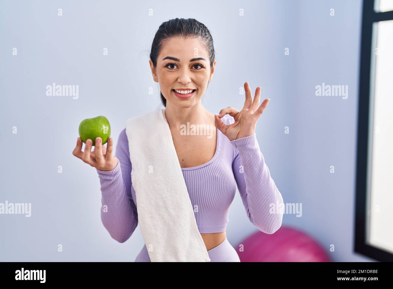 Young woman wearing sportswear and towel eating green apple doing ok ...