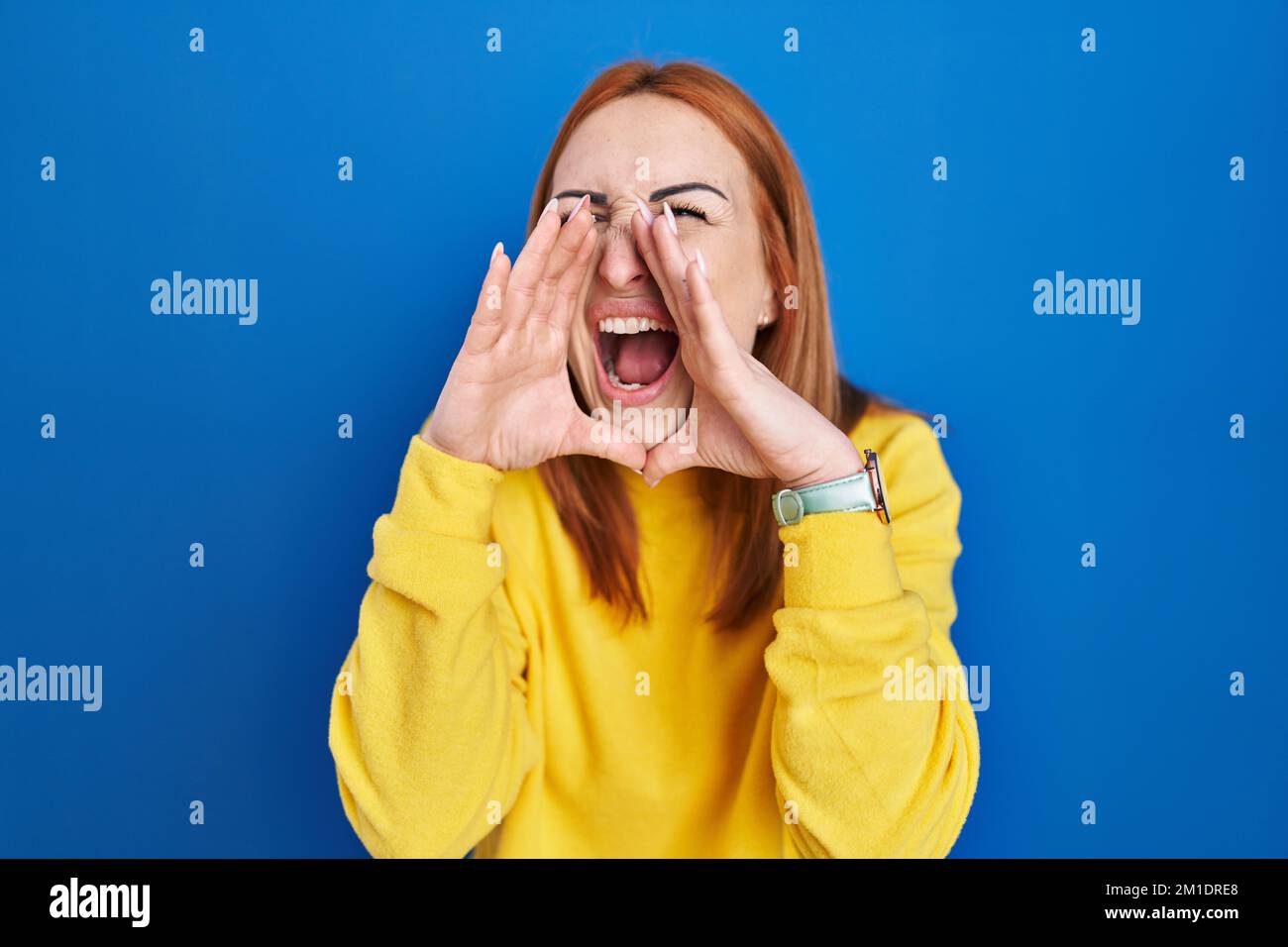 Young woman standing over blue background shouting angry out loud with ...