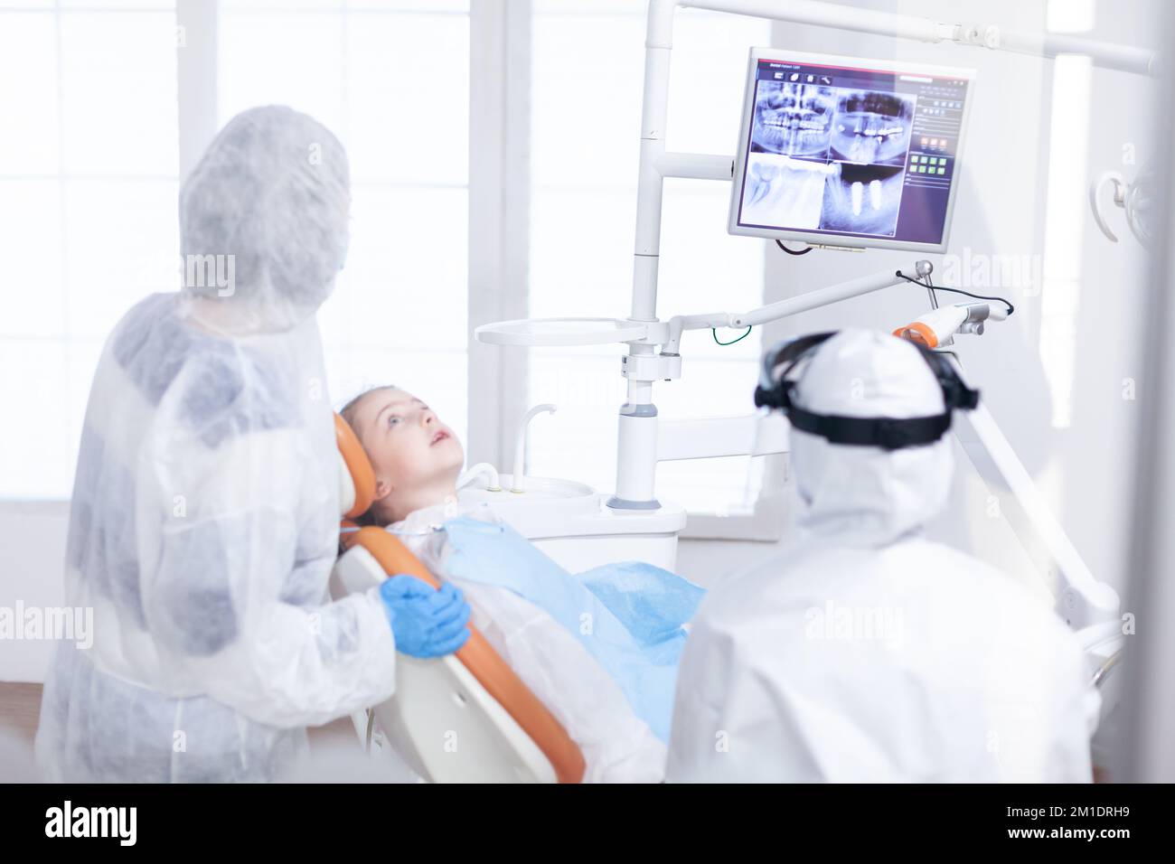 Little girl in ppe looking at her mother in the course of dental ...