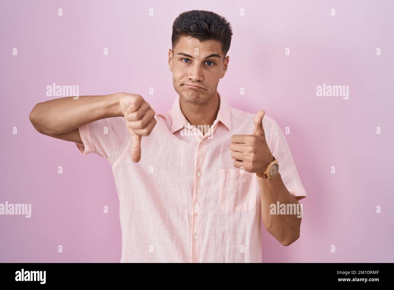 Young hispanic man standing over pink background doing thumbs up and ...