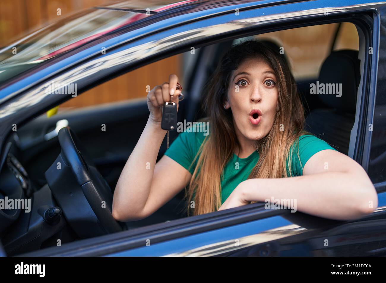 Young brunette woman holding key of new car scared and amazed with open ...