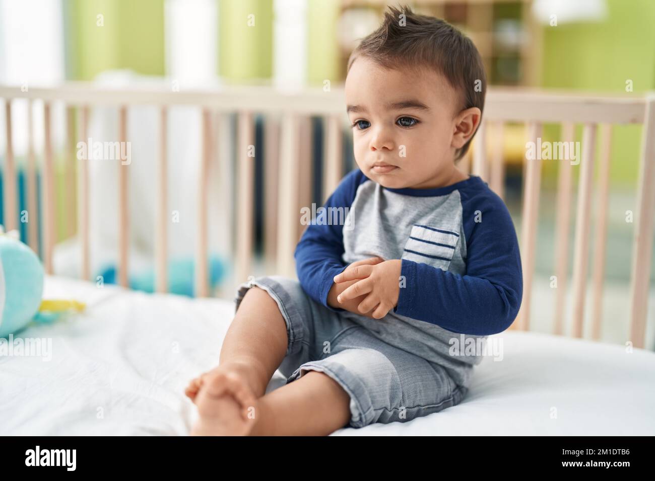 Adorable hispanic toddler sitting on cradle with relaxed expression at ...