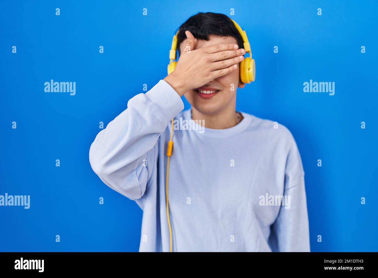 Non binary person listening to music using headphones smiling and ...