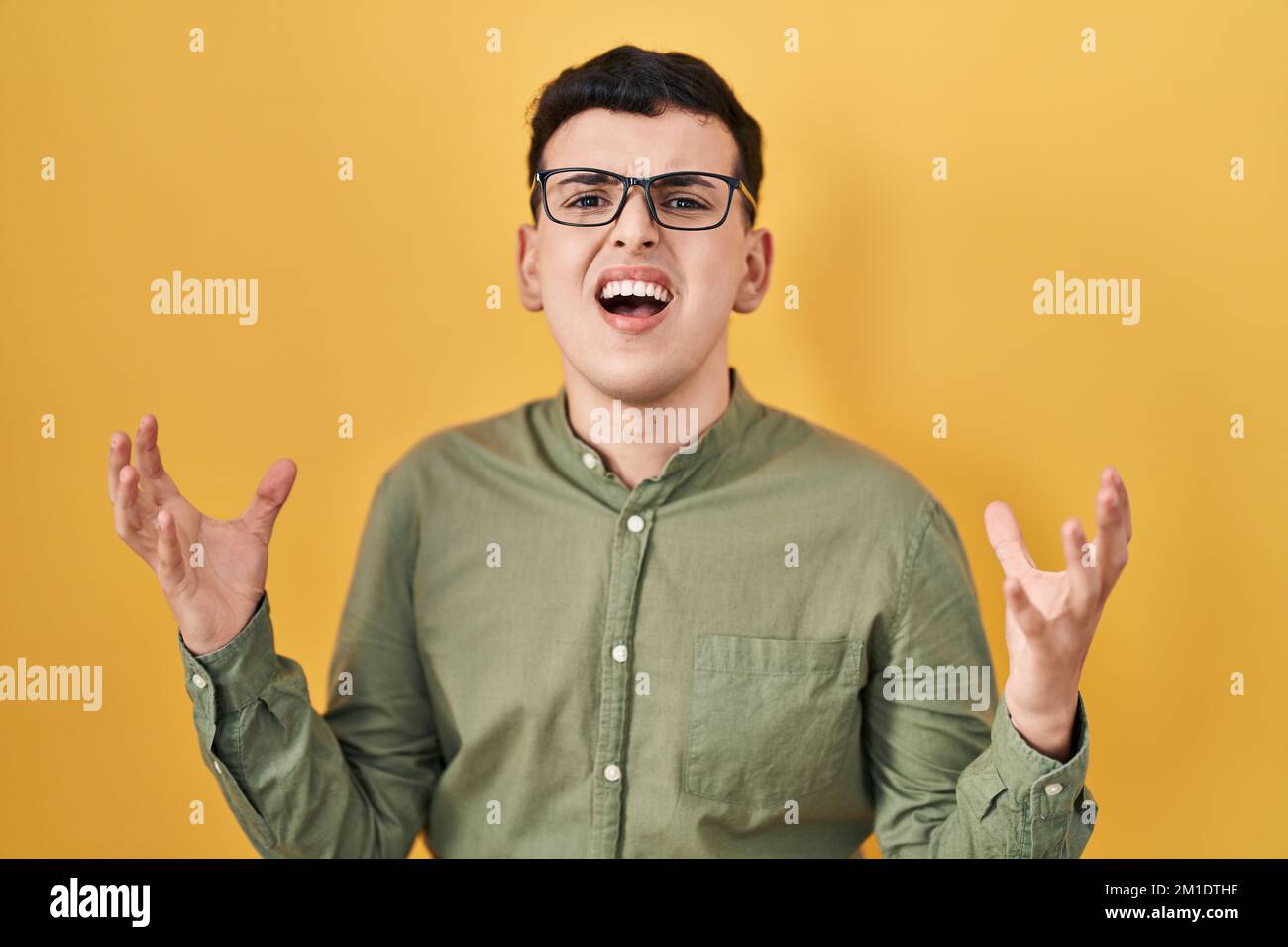 Non binary person standing over yellow background crazy and mad ...