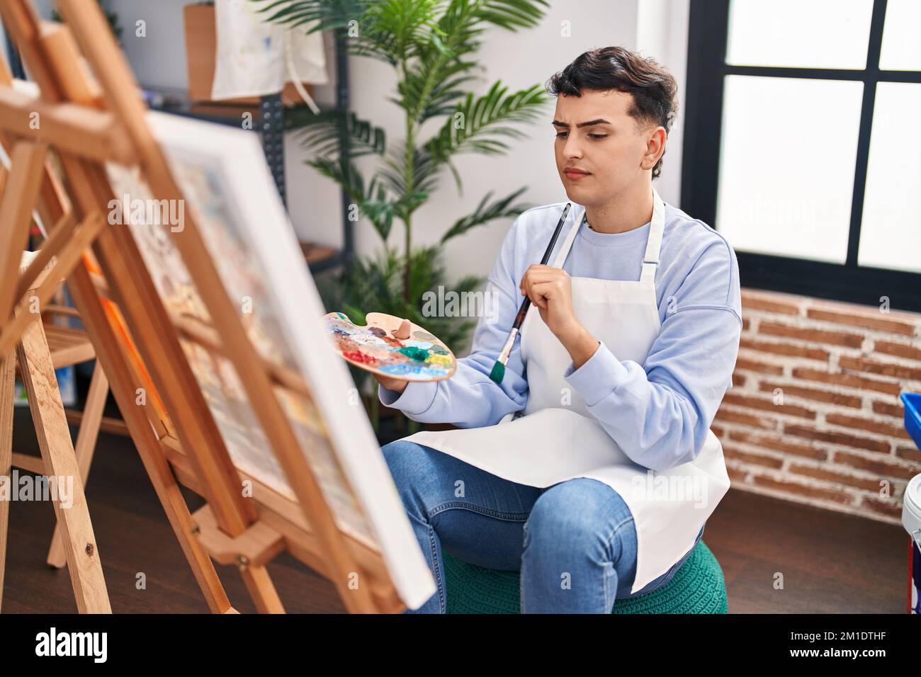 Young non binary man artist drawing with doubt expression at art studio ...