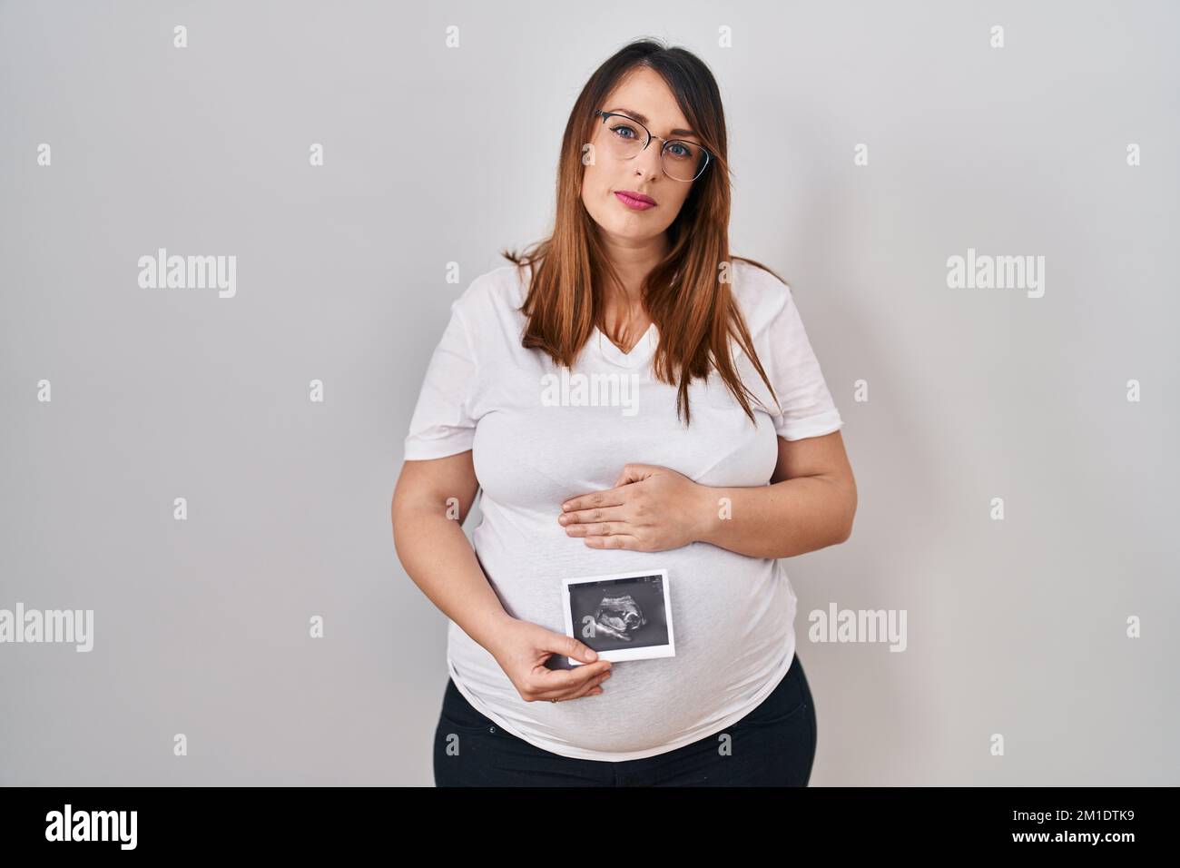 Pregnant woman holding baby ecography relaxed with serious expression ...