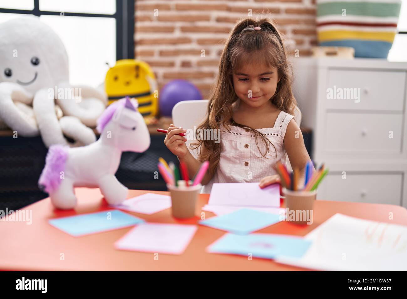 Adorable hispanic girl student sitting on table drawing on paper at ...