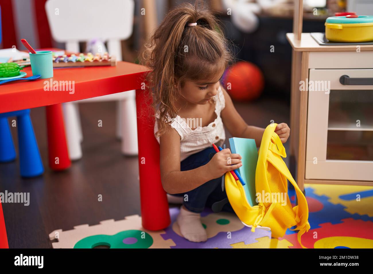 Adorable hispanic girl preschool student sitting on floor holding book ...