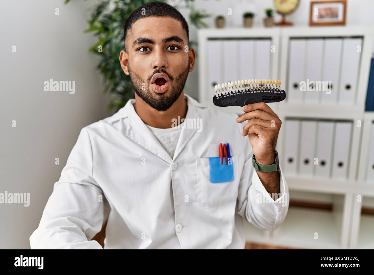 Young indian man holding teeth whitening palette scared and amazed with ...