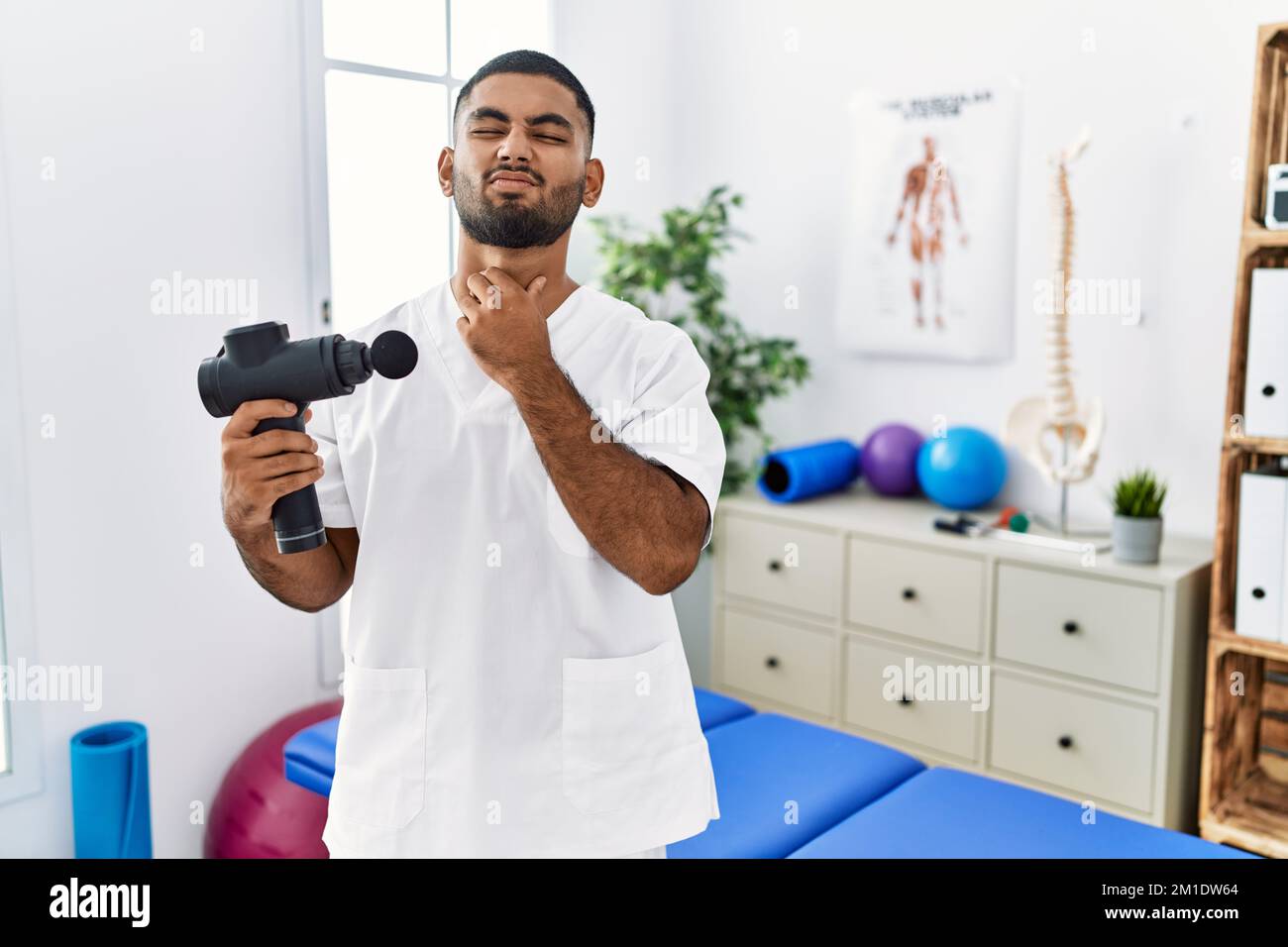 Young indian physiotherapist holding therapy massage gun at wellness ...