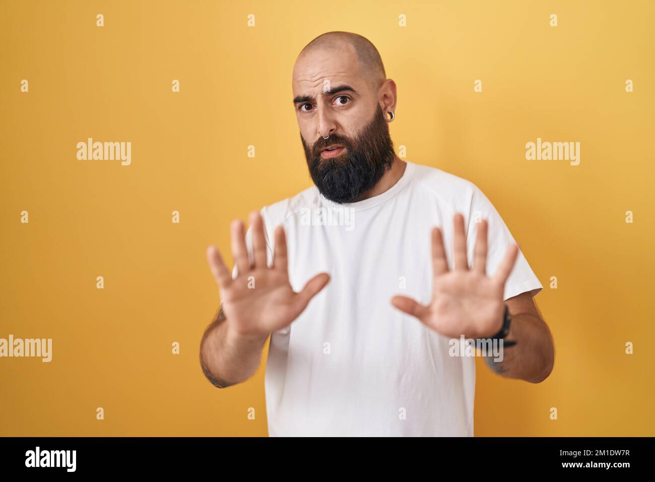 Young hispanic man with beard and tattoos standing over yellow ...