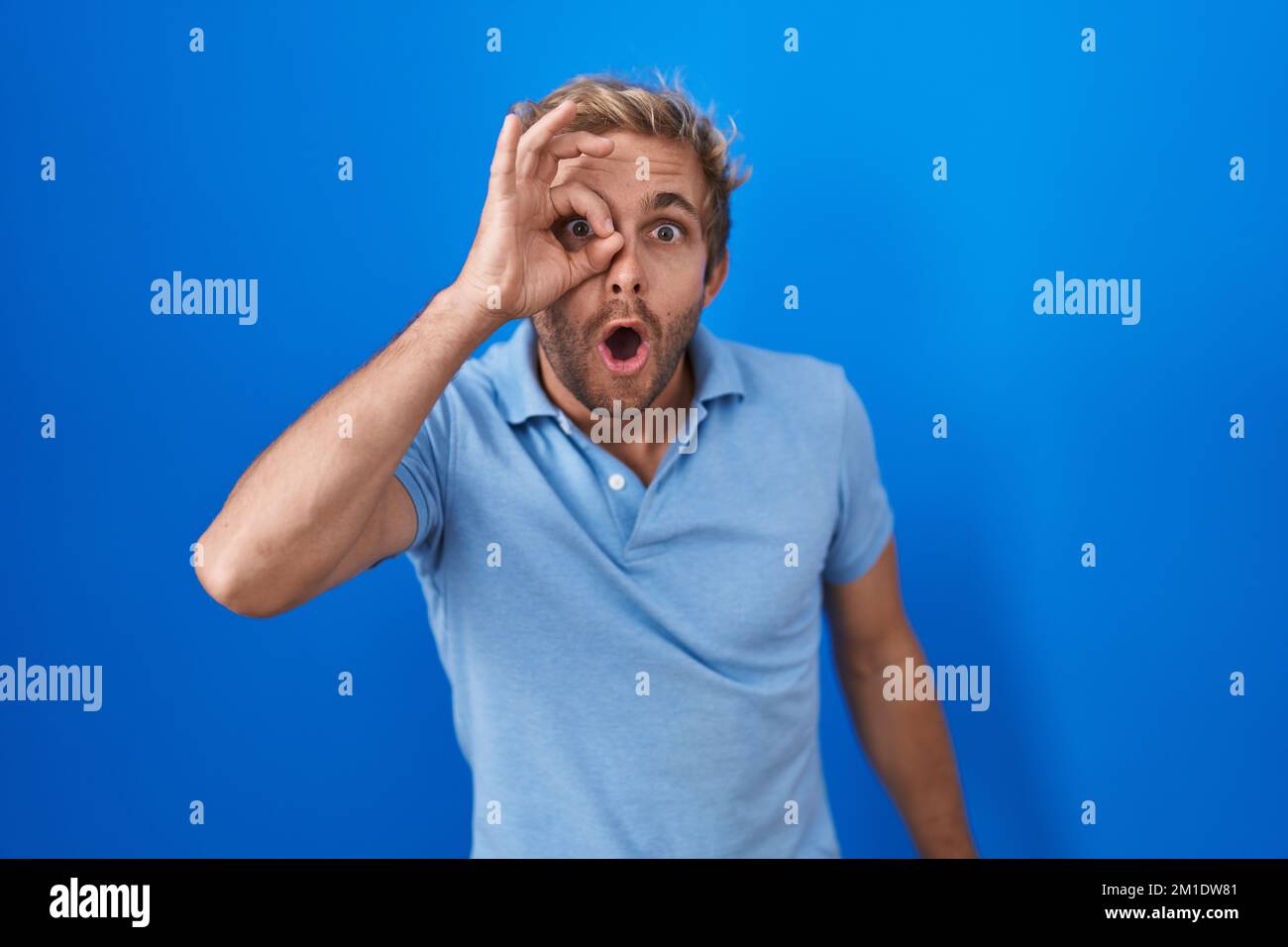 Caucasian man standing over blue background doing ok gesture shocked ...
