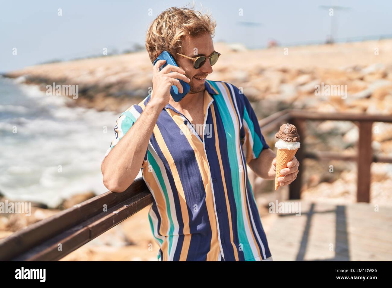 Young man tourist talking on the smartphone eating ice cream at seaside ...
