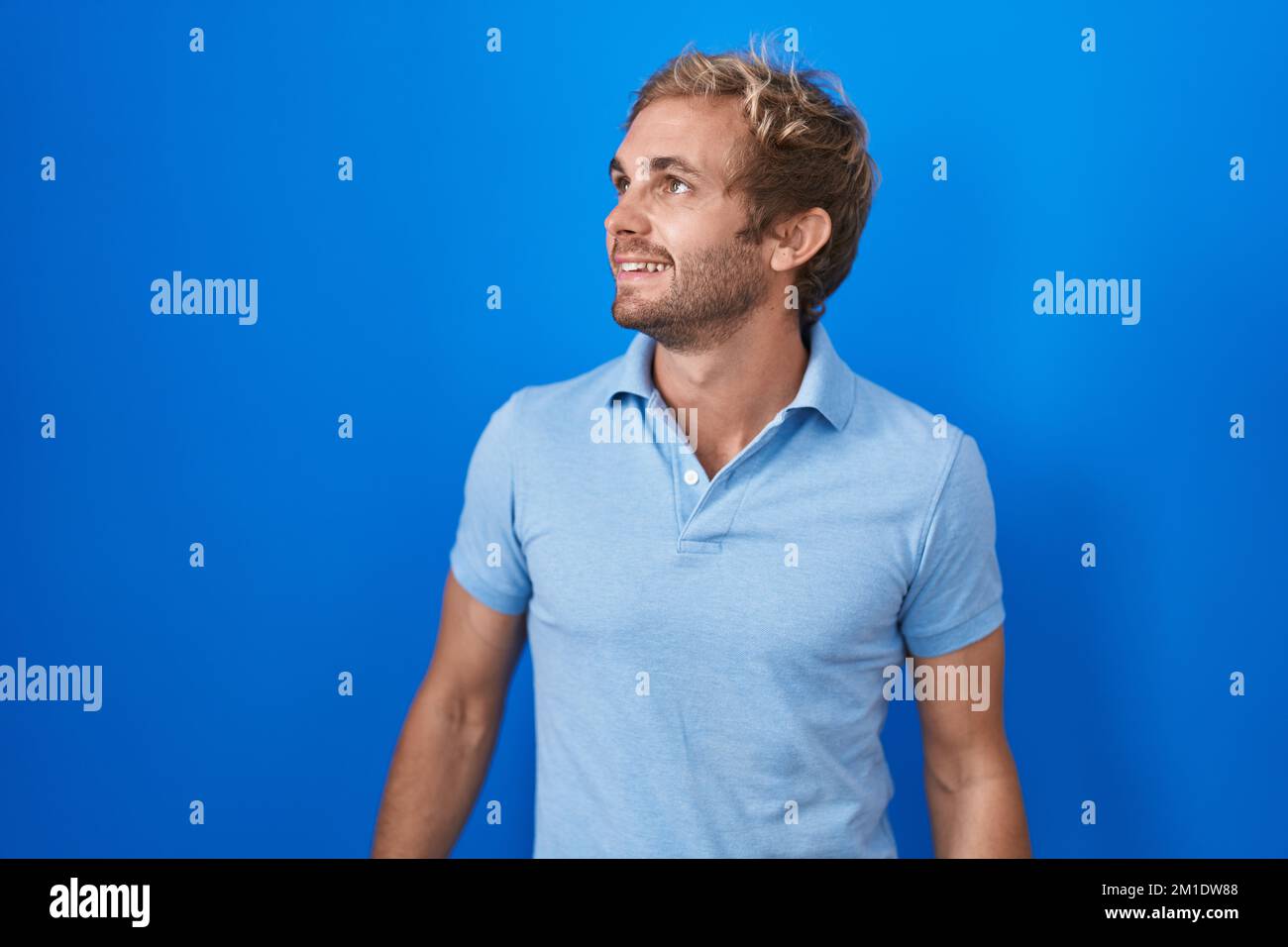 Caucasian man standing over blue background looking away to side with ...