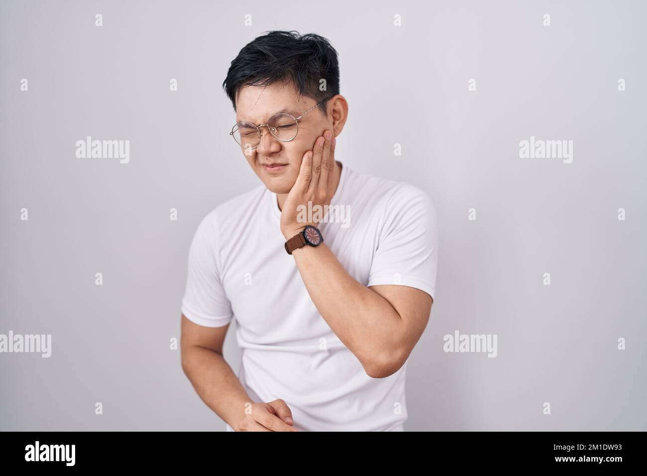 Young asian man standing over white background touching mouth with hand ...