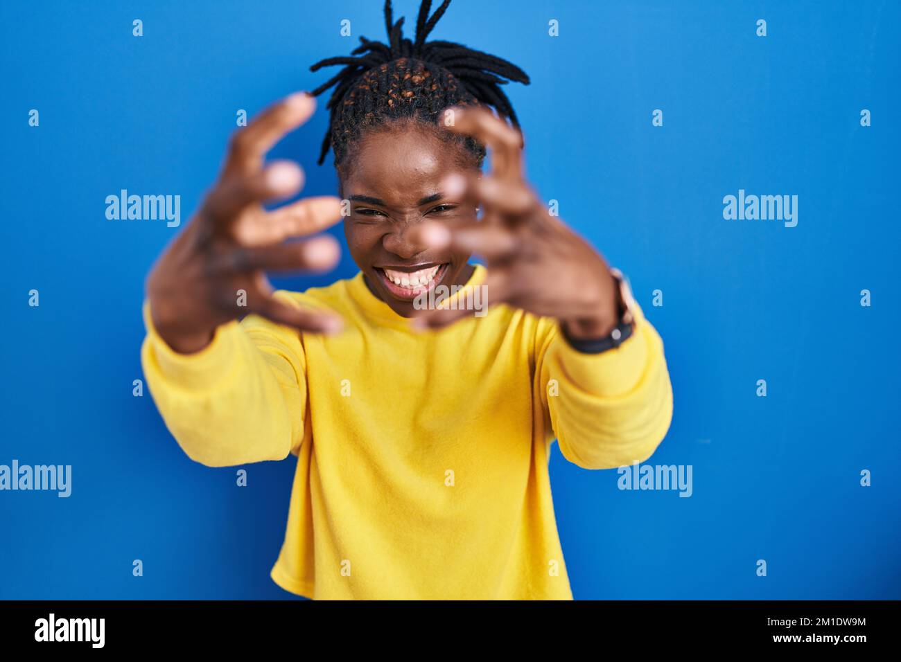 Beautiful black woman standing over blue background shouting frustrated ...